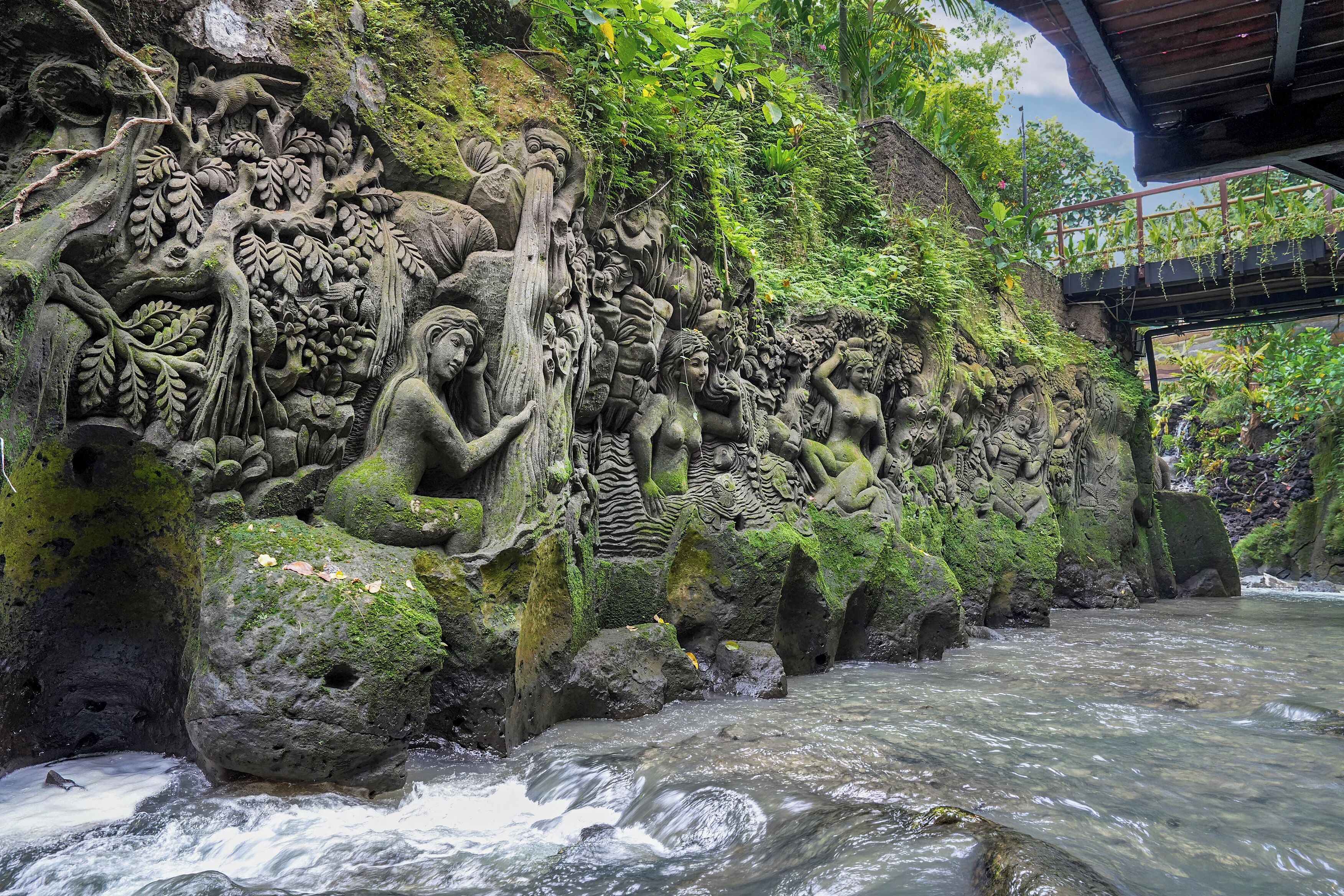 Mural de pedra com esculturas, um rio e uma ponte.