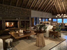 Uma sala de estar acolhedora com lareira de pedra, móveis de madeira e teto alto com telhado de palha.