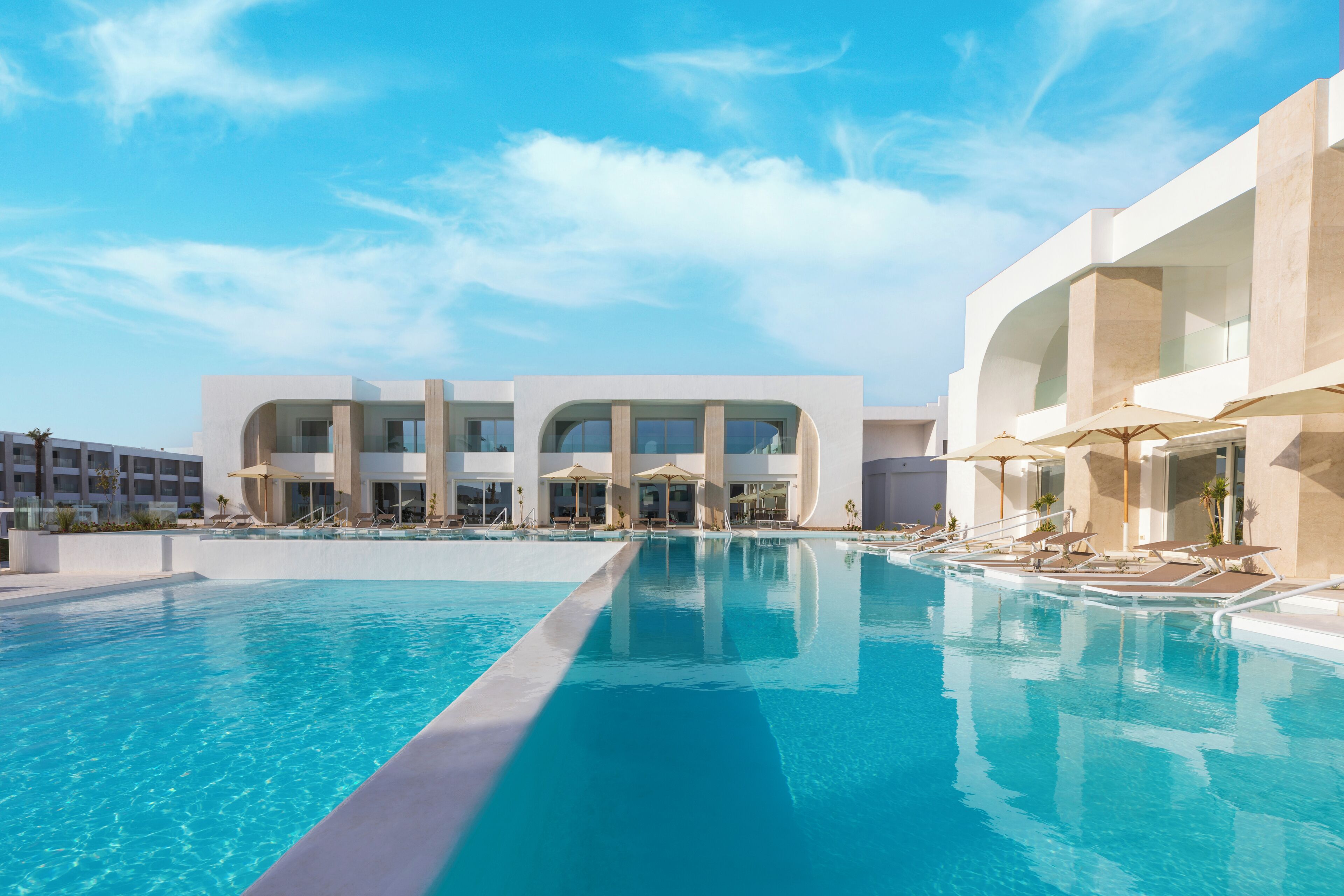 Um hotel moderno com uma piscina grande, espreguiçadeiras e guarda-sóis.