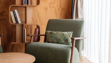 Uma poltrona verde com uma almofada estampada, uma estante de madeira com livros e uma mesa redonda de madeira.
