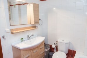 Um banheiro moderno com pia branca, penteadeira de madeira, um espelho e vaso sanitário.