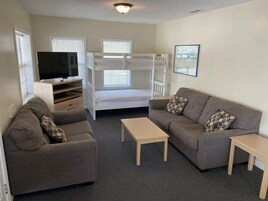 Um quarto mobiliado com uma cama de solteiro, um sofá, uma mesa de centro, uma televisão e uma estante.