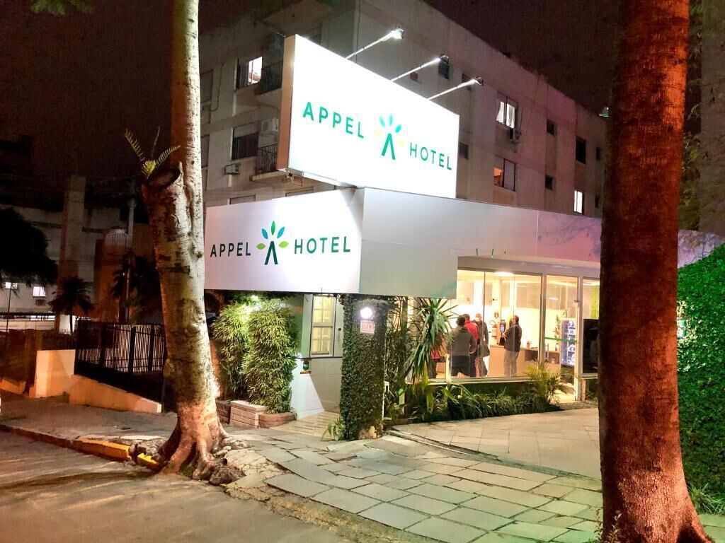 Um hotel chamado 'APPEL HOTEL' com uma placa, uma entrada bem iluminada e um passeio pavimentado.