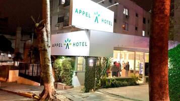 Um hotel chamado 'APPEL HOTEL' com uma placa, uma entrada bem iluminada e um passeio pavimentado.