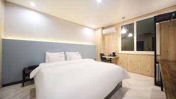 Quarto de hotel moderno com uma cama grande, uma pequena mesa com cadeira e uma janela com vista.
