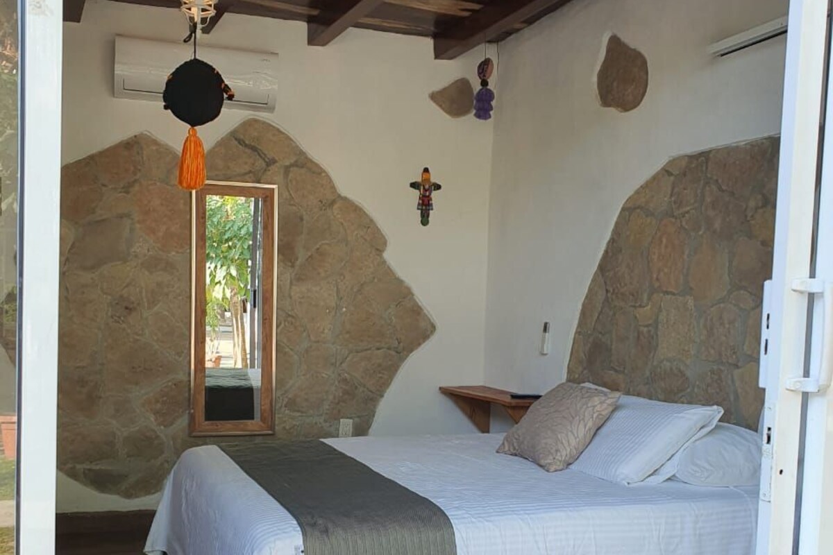 Quarto com cama, mesa de cabeceira, luminária pendente e parede de pedra.
