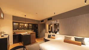 Quarto de hotel moderno com uma cama grande, área de estar separada, cozinha compacta e banheiro.