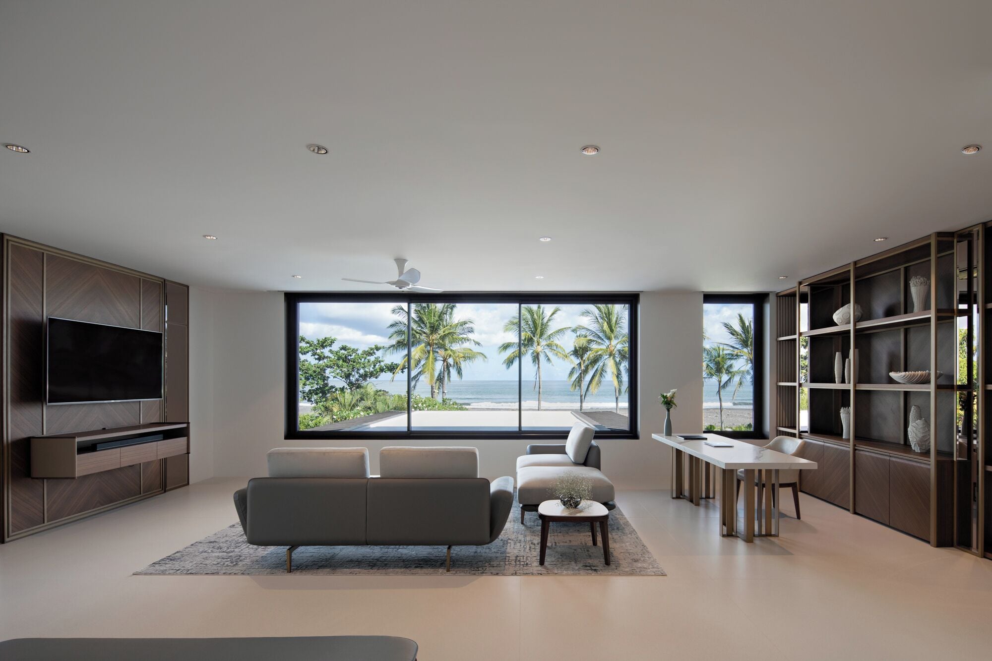 Uma sala de estar moderna com uma televisão grande, assentos confortáveis, um espaço para refeições e vista para a praia.