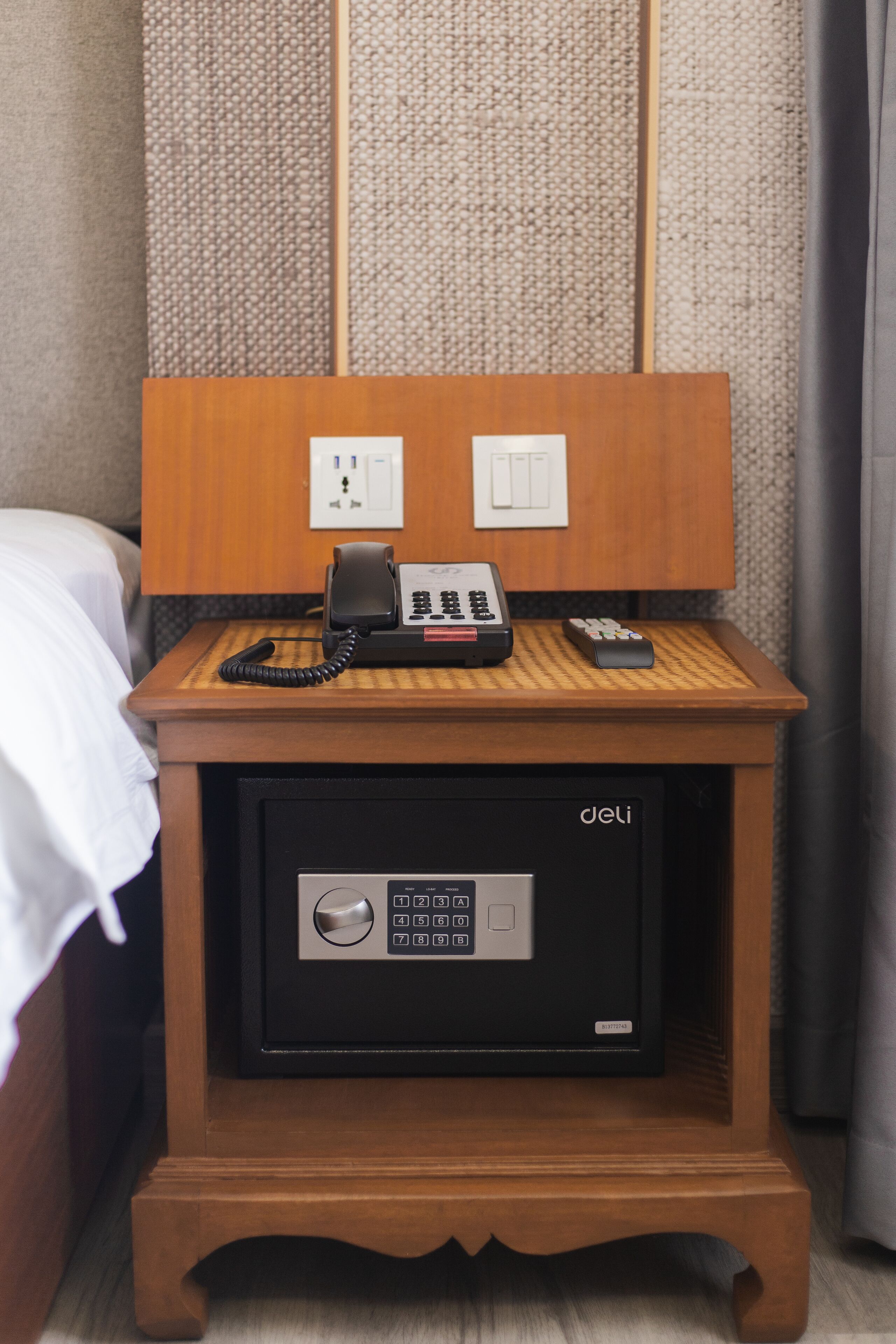 Uma mesa de cabeceira de madeira com um telefone, um controle remoto e um minibar com o cartão-chave do minibar.