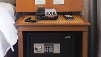 Uma mesa de cabeceira de madeira com um telefone, um controle remoto e um minibar com o cartão-chave do minibar.