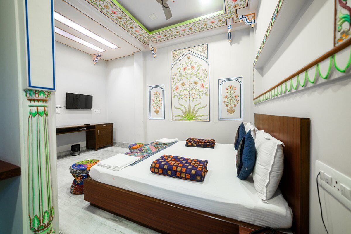 Quarto com cama, almofadas, televisão e escrivaninha.