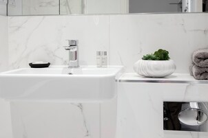 Casa de banho moderna com uma pia de mármore branco, uma pequena tigela preta, um vaso branco com uma planta e uma toalha.