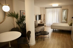 Quarto de hotel moderno com sofá, cama, televisão, mesinha e planta em vaso.