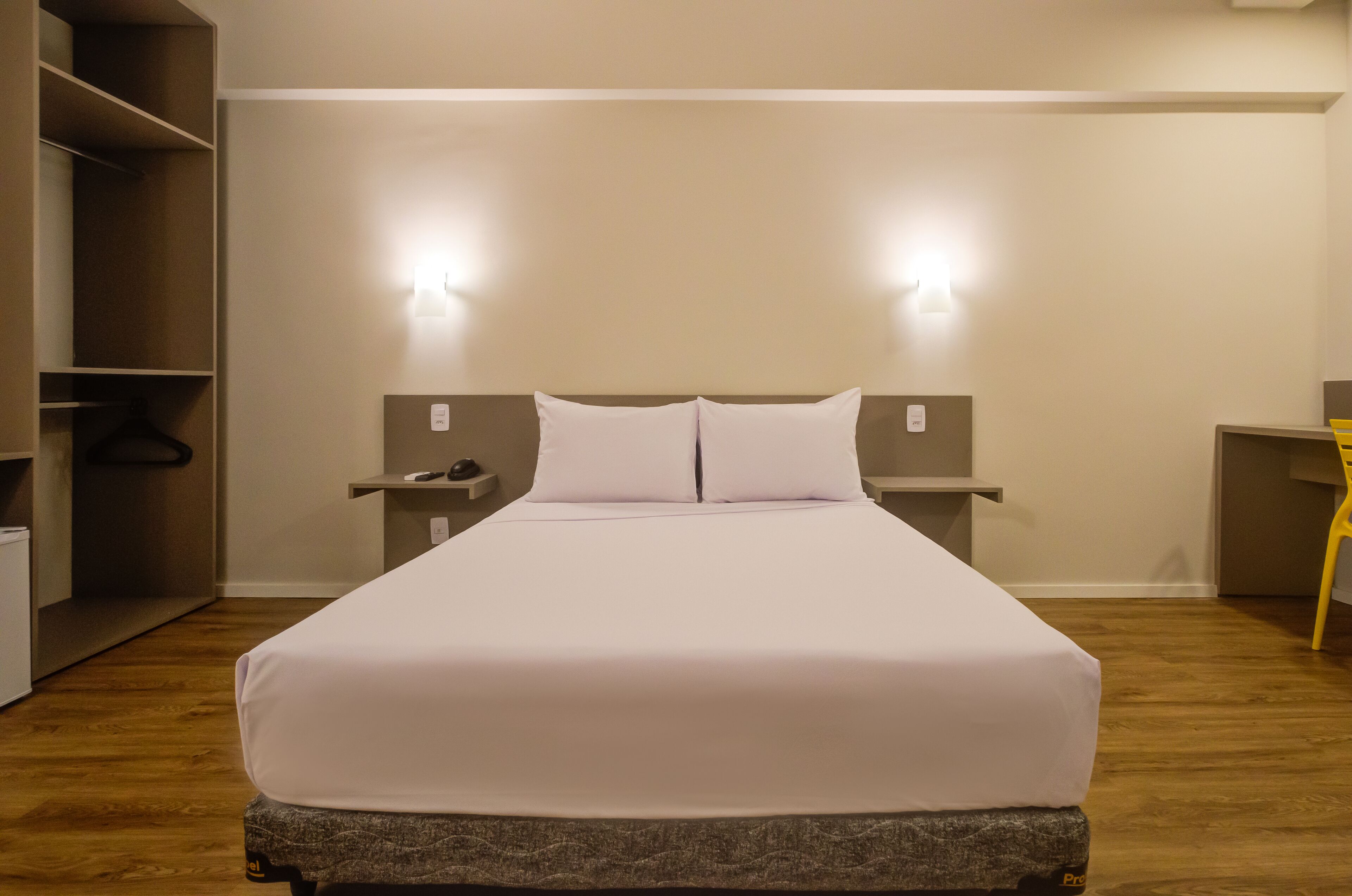 Quarto de hotel com uma cama grande, duas mesas de cabeceira, um criado-mudo e um guarda-roupa.