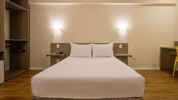 Quarto de hotel com uma cama grande, duas mesas de cabeceira, um criado-mudo e um guarda-roupa.