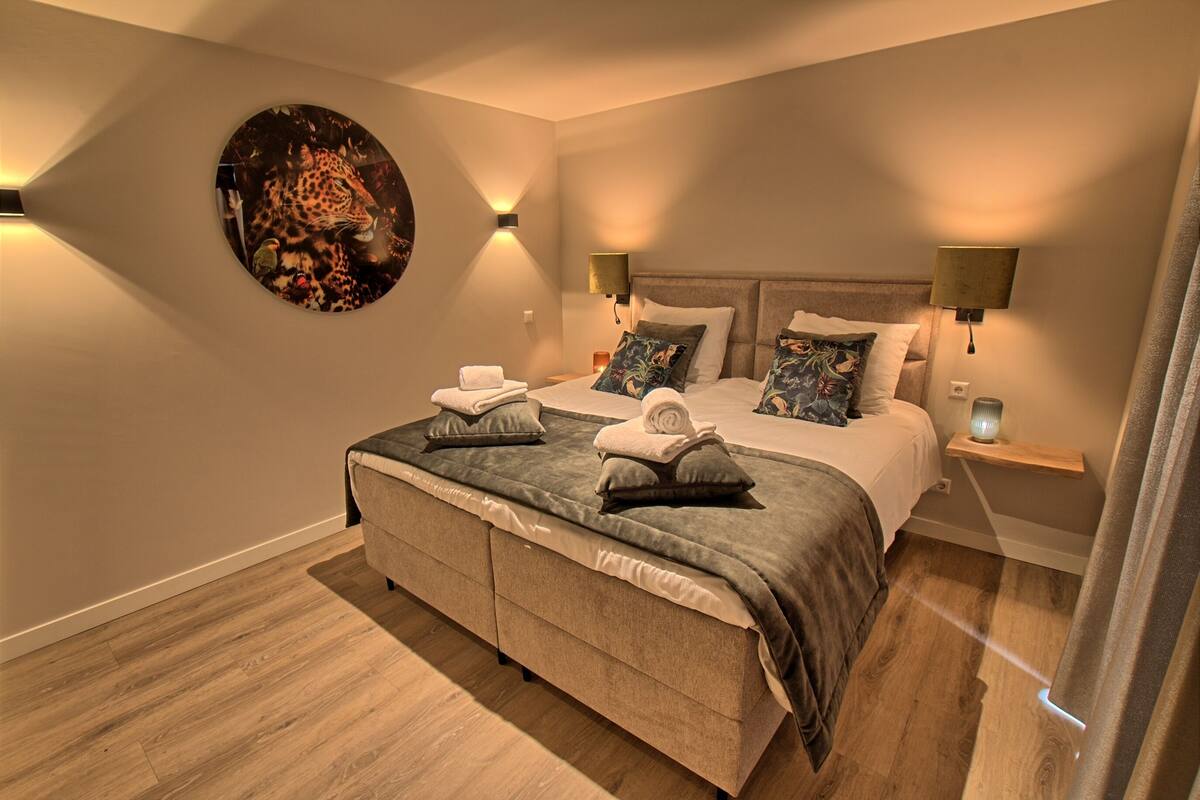 Quarto moderno com uma cama grande, duas mesas de cabeceira e uma obra de arte na parede.