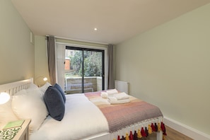 Quarto de hotel com uma cama, mesa de cabeceira e vista para uma parede de tijolos e vegetação lá fora.