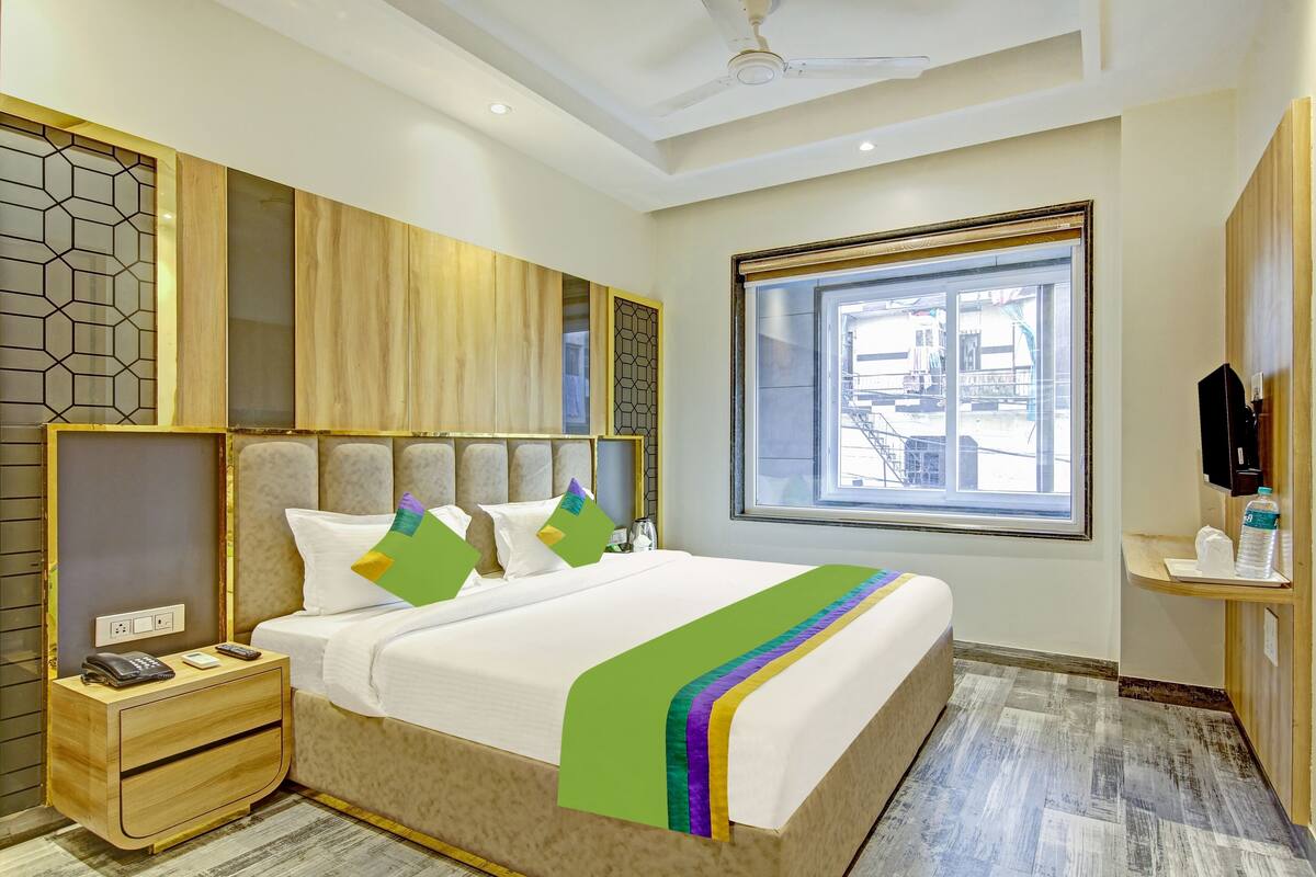 Quarto de hotel com cama, mesa de cabeceira, janela e vista para edifícios.