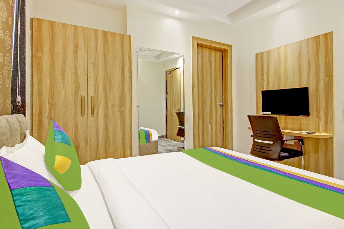 Quarto de hotel com cama, escrivaninha, cadeira, televisão e armários de madeira.