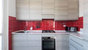 Cozinha moderna com eletrodomésticos de aço inoxidável, mosaico de azulejos vermelhos e armários de madeira.