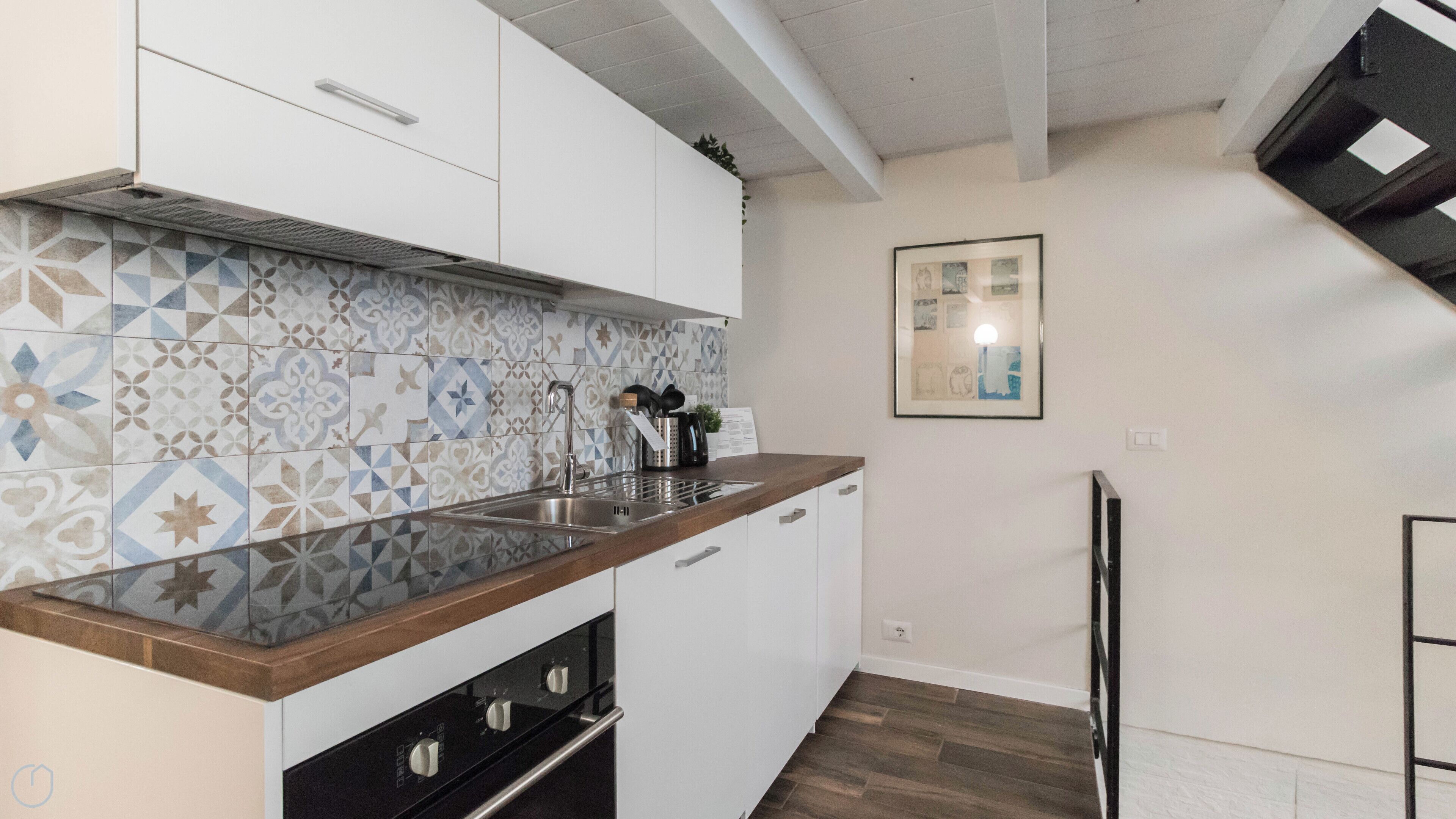 Cozinha moderna com azulejos estampados no painel, eletrodomésticos de aço inoxidável e bancadas de madeira.