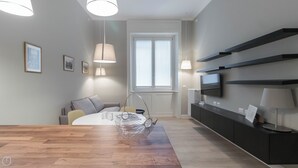 Uma sala de estar moderna com uma mesa de jantar de madeira, um sofá e uma televisão fixada na parede.