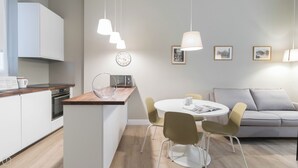 Uma cozinha moderna com bancada de madeira, micro-ondas e cesta. Há uma área de jantar com mesa redonda, cadeiras e sofá.