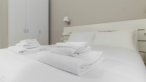Cama bem arrumada com toalhas brancas dobradas e cabeceira branca em quarto de hotel.