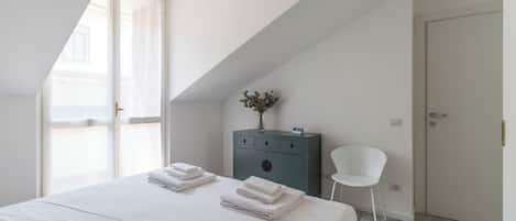 Quarto com uma cama, cômoda, cadeira e janela.