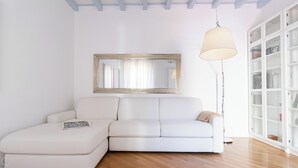 Um sofá branco com um espelho decorativo acima, uma luminária de chão e um armário branco com portas de vidro.