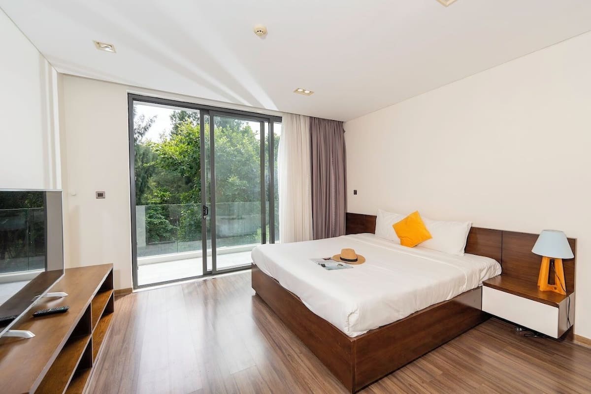 Quarto de hotel moderno com uma cama grande, uma escrivaninha com televisão e uma porta de vidro deslizante para o exterior.