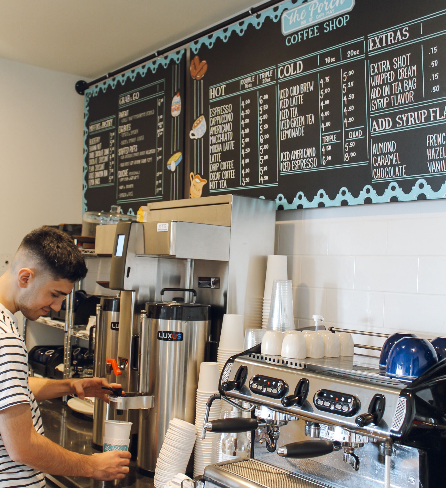 Uma cafeteria com cardápio, máquina de café expresso e xícaras de café.