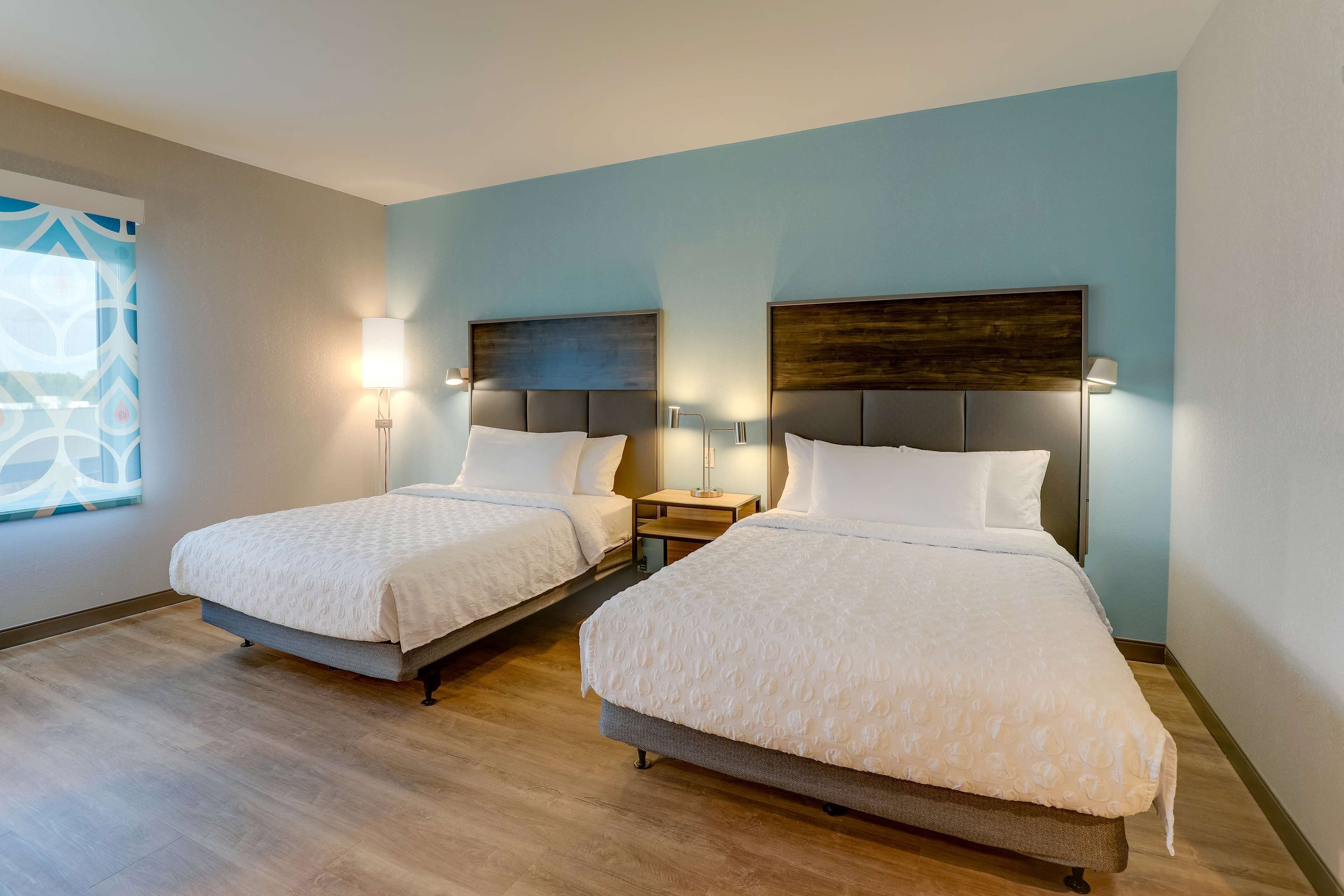 Quarto de hotel com duas camas, cada uma com cabeceira, mesas de cabeceira e luminárias.