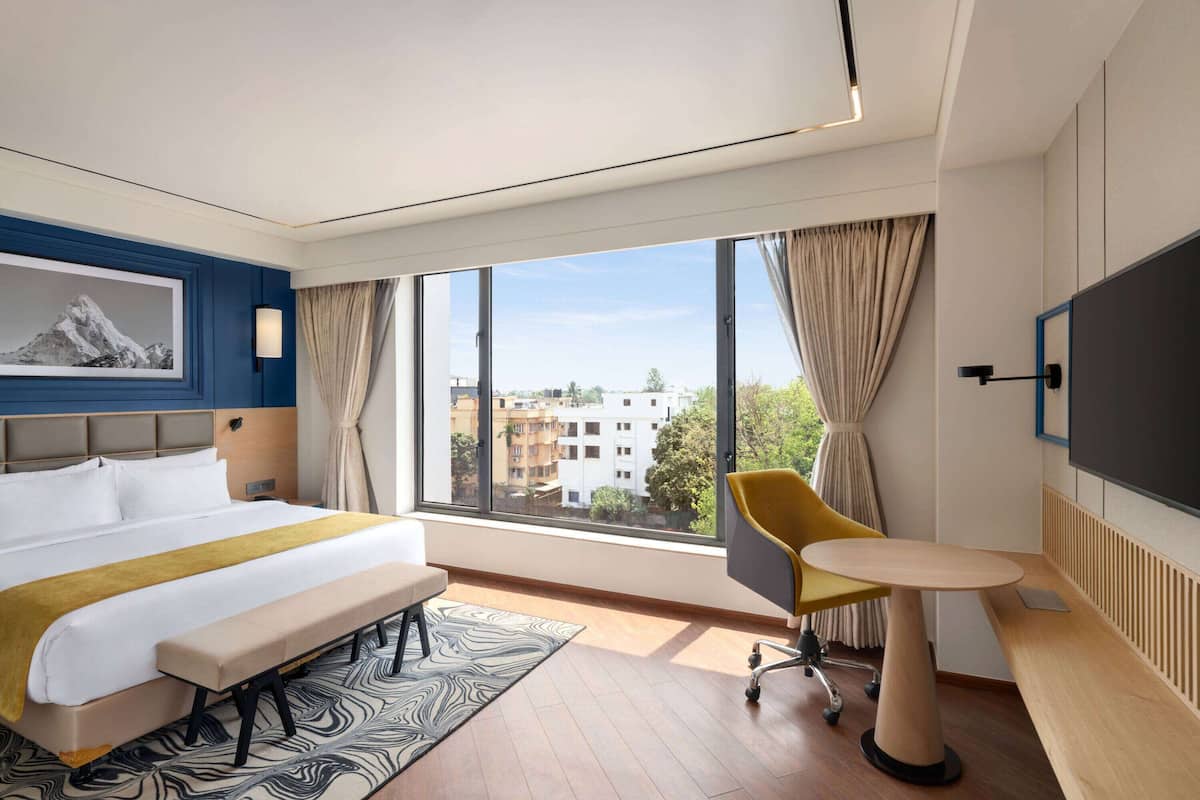 Quarto de hotel com uma cama grande, uma escrivaninha com cadeira, uma televisão e uma janela com vista para a cidade.