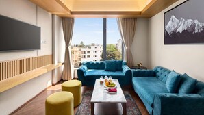 Sala de estar moderna com uma televisão grande, um sofá azul, uma mesa de centro com frutas e vista para a cidade.