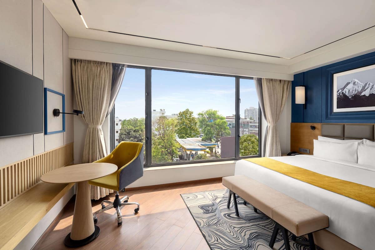 Quarto de hotel moderno com uma janela grande, uma cama, uma mesa e uma cadeira.
