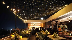 Restaurante ao ar livre com luzes de fada, mesas com centros de mesa florais e um bar.