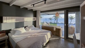 Quarto moderno com uma cama grande, cabeceira com prateleira embutida, vista do oceano através de uma porta de vidro deslizante e luminária pendente.