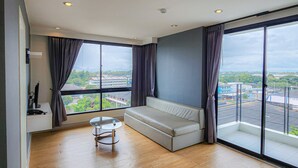 Quarto moderno com uma janela grande, um sofá, uma mesa pequena e uma televisão.