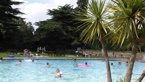 Piscina com pessoas na água, cercada por árvores e um muro de pedra.