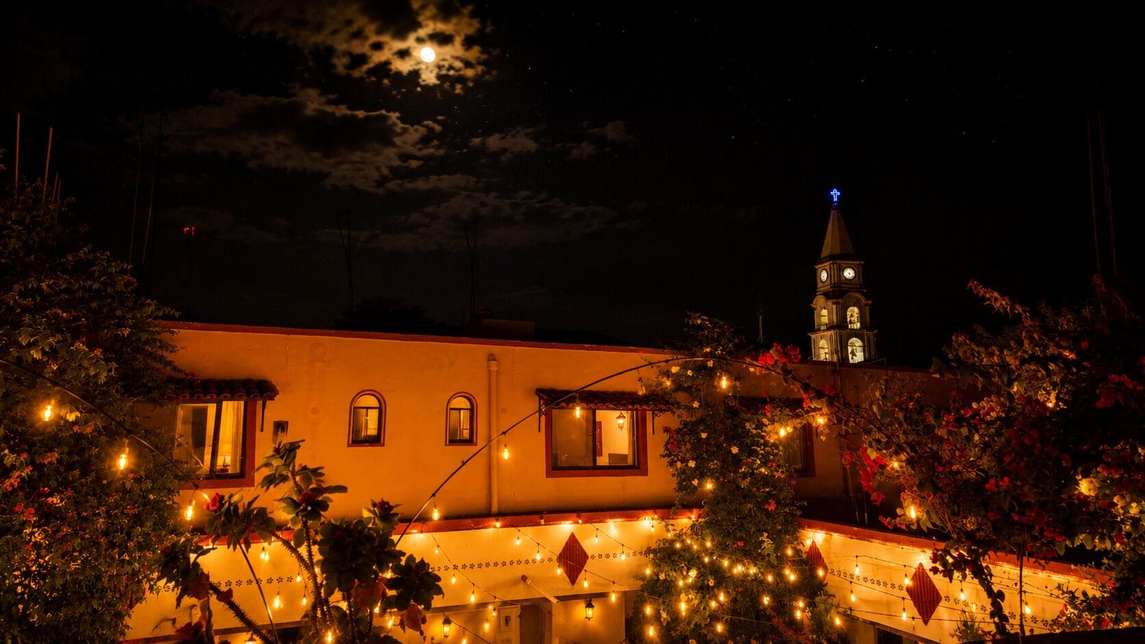 Um edifício com uma torre de relógio, luzes de corda e uma lua no céu.