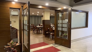 Um hall de hotel moderno com painéis de madeira, um tapete vermelho e uma área de refeições com mesas e cadeiras.