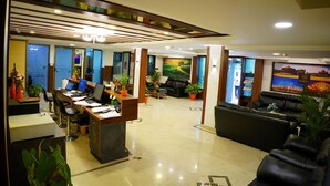 Um lobby de hotel moderno com balcão de recepção, área de estar e uma grande janela com vista para a cidade.