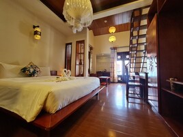 Um quarto espaçoso com cama grande, piso de madeira, um candelabro e uma escada que leva a outro cômodo.