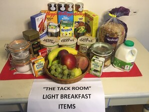 Uma mesa com diversos itens de pequeno-almoço, incluindo cereais, frutas e produtos lácteos.