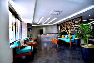 Uma área de recepção de hotel com balcão, espaço para sentar e amplas janelas.