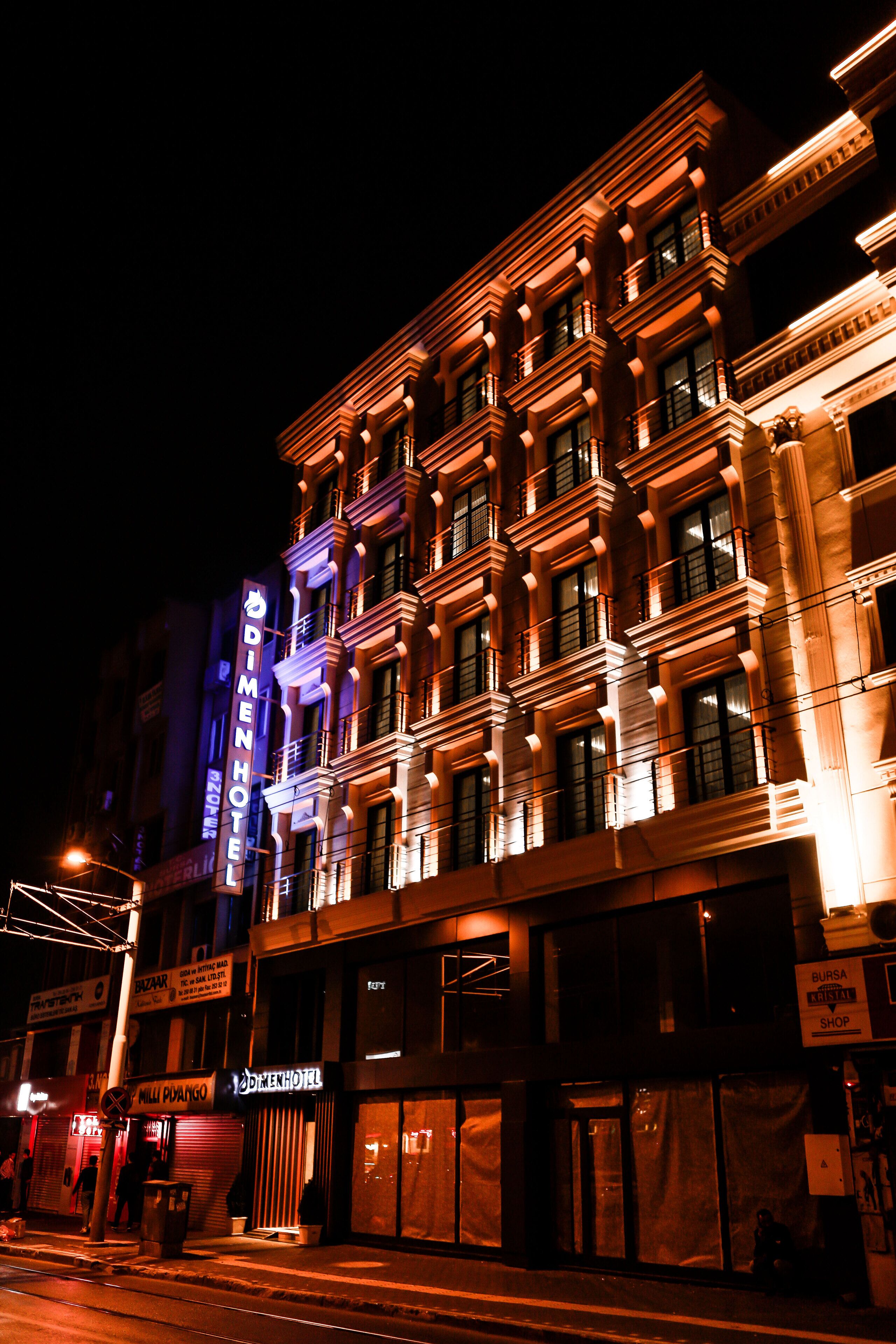 Um edifício de vários andares com um destaque para a placa 'DIMENHOTEL', apresentando um estilo arquitetônico clássico com detalhes ornamentais e várias varandas.