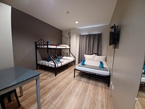 Quarto com beliches, sofá-cama, televisão na parede e uma mesa.
