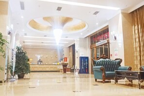 Um saguão de hotel com balcão de recepção, um sofá azul e um lustre grande.