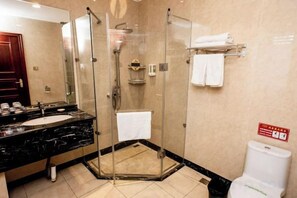 Casa de banho de hotel com chuveiro em cabine de vidro, lavatório com bancada preta e sanita branca.